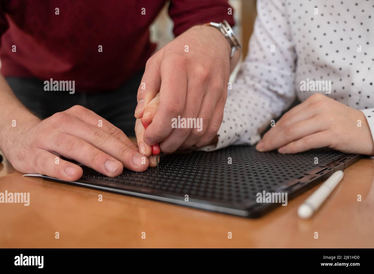 A man teaches a woman how to use a special stencil and stylus to write ...