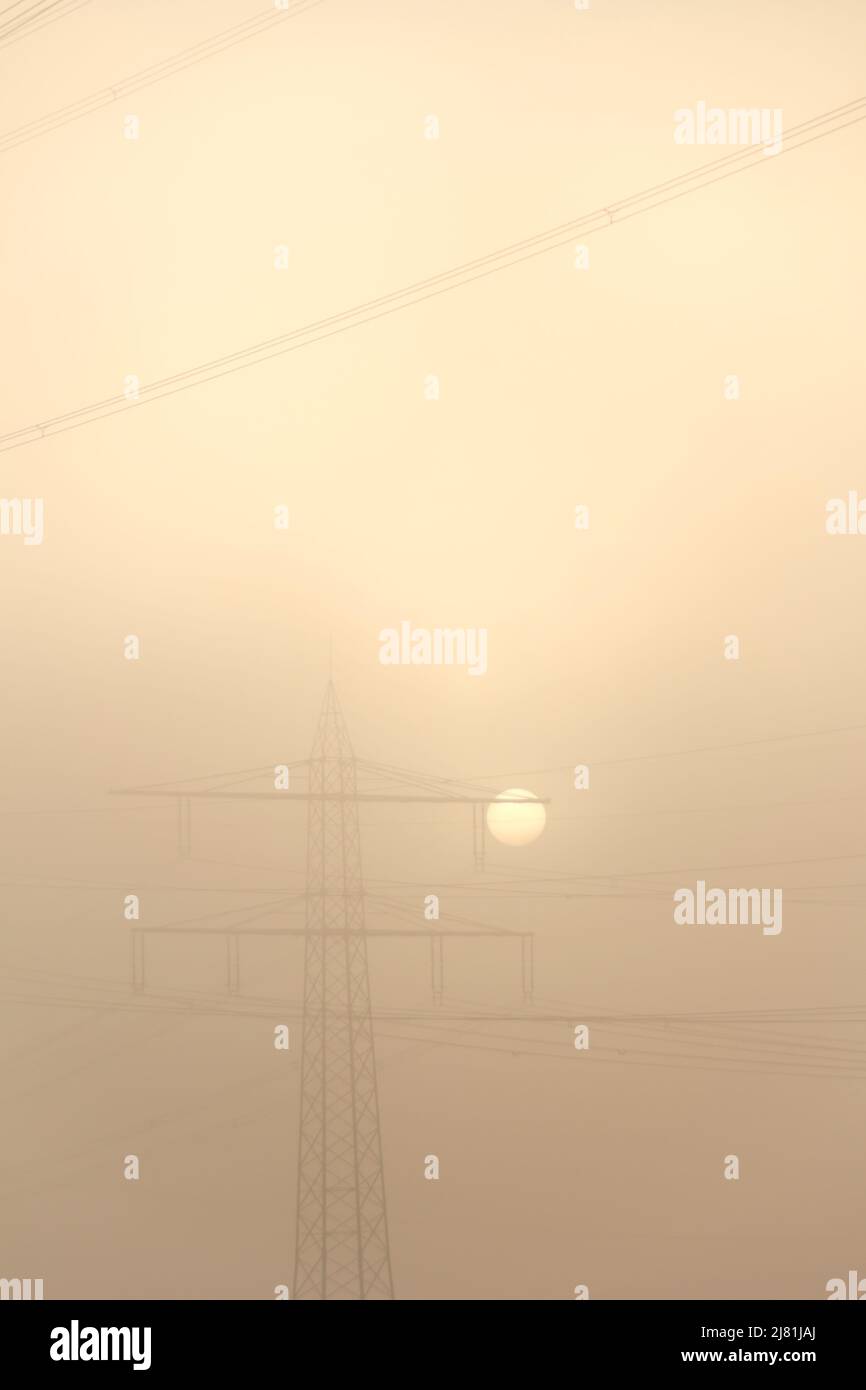 Sun in the mist behind a power pole with the orange sky in the ...