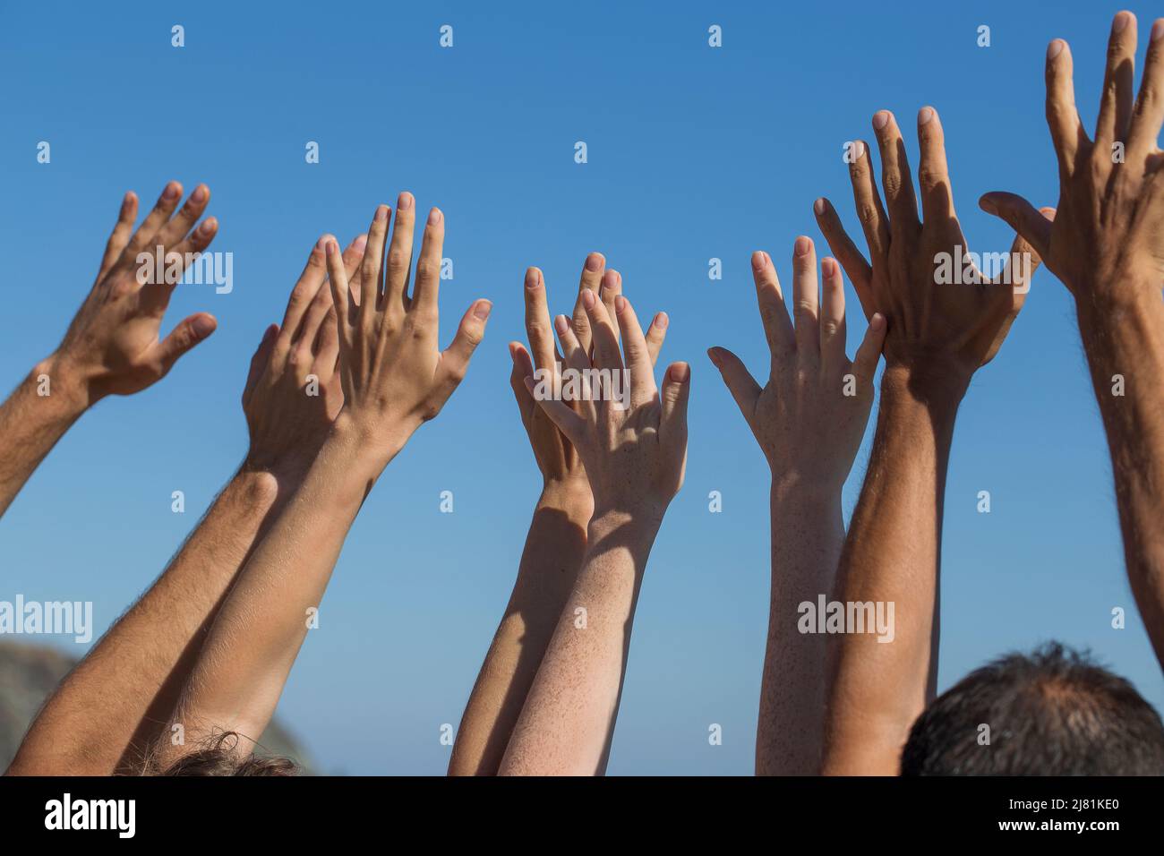 Group of people raise hands in air across blue sky, close up Stock ...
