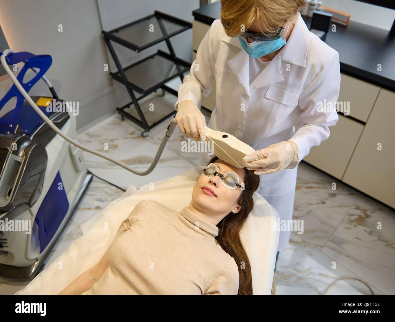 Overhead view of a woman getting facial laser treatment for hair ...