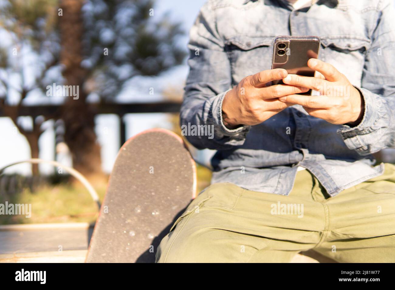 Adult man texting his friends on his phone sitting with his skateboard ...