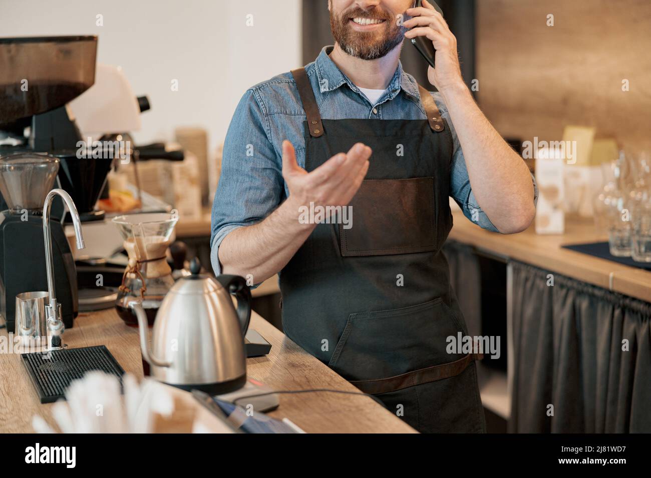 Smiling barista talks phone standing behind counter at coffee shop ...