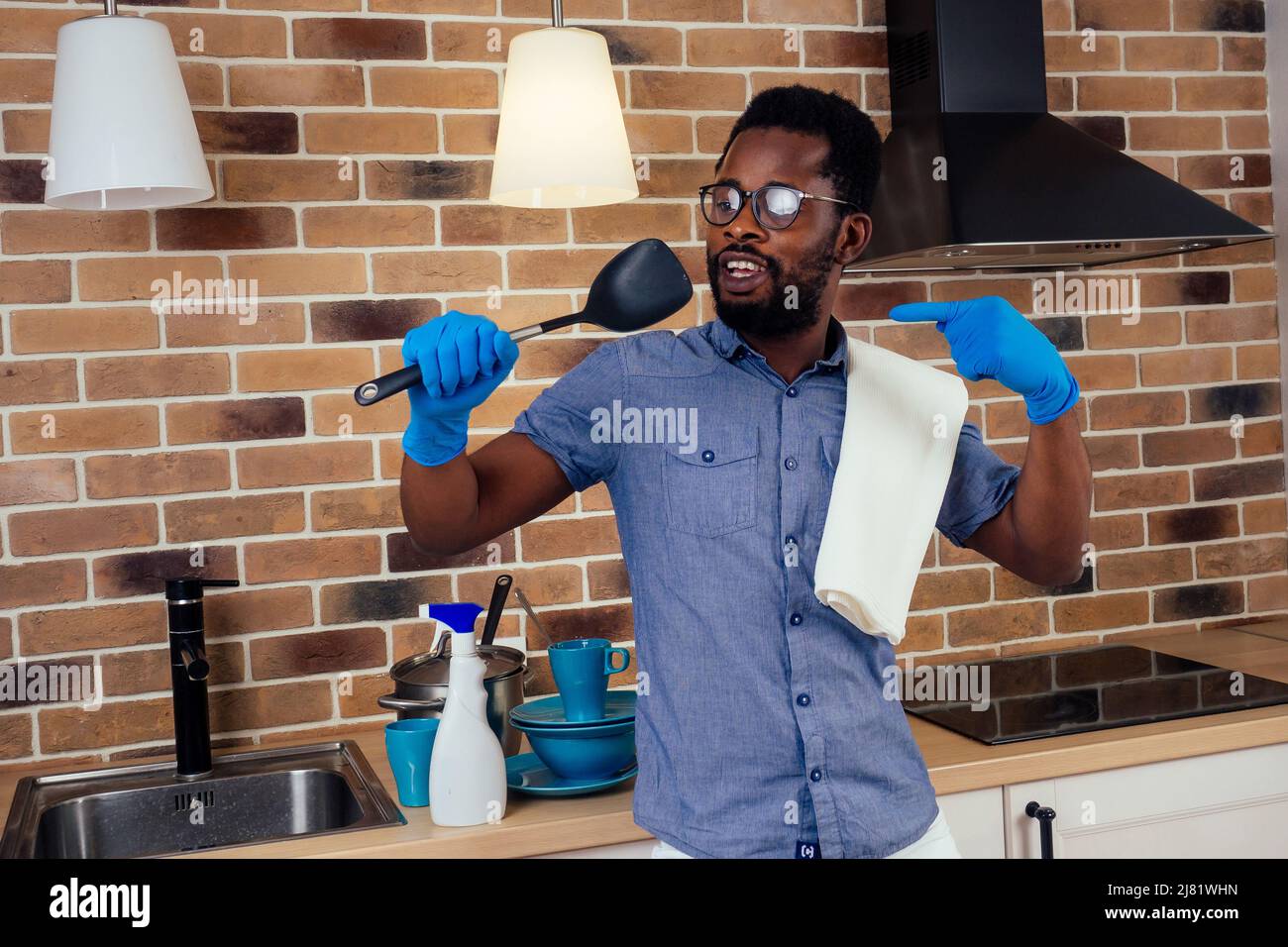 african man cleaning cooktop cooker hood and singing at kitchen spoon ...