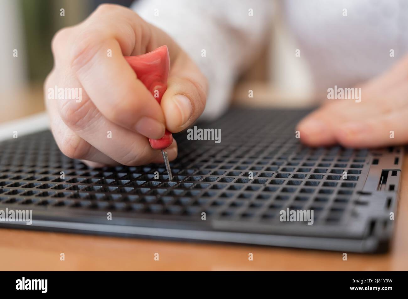 A woman uses a special stencil and stylus to write a letter in braille ...