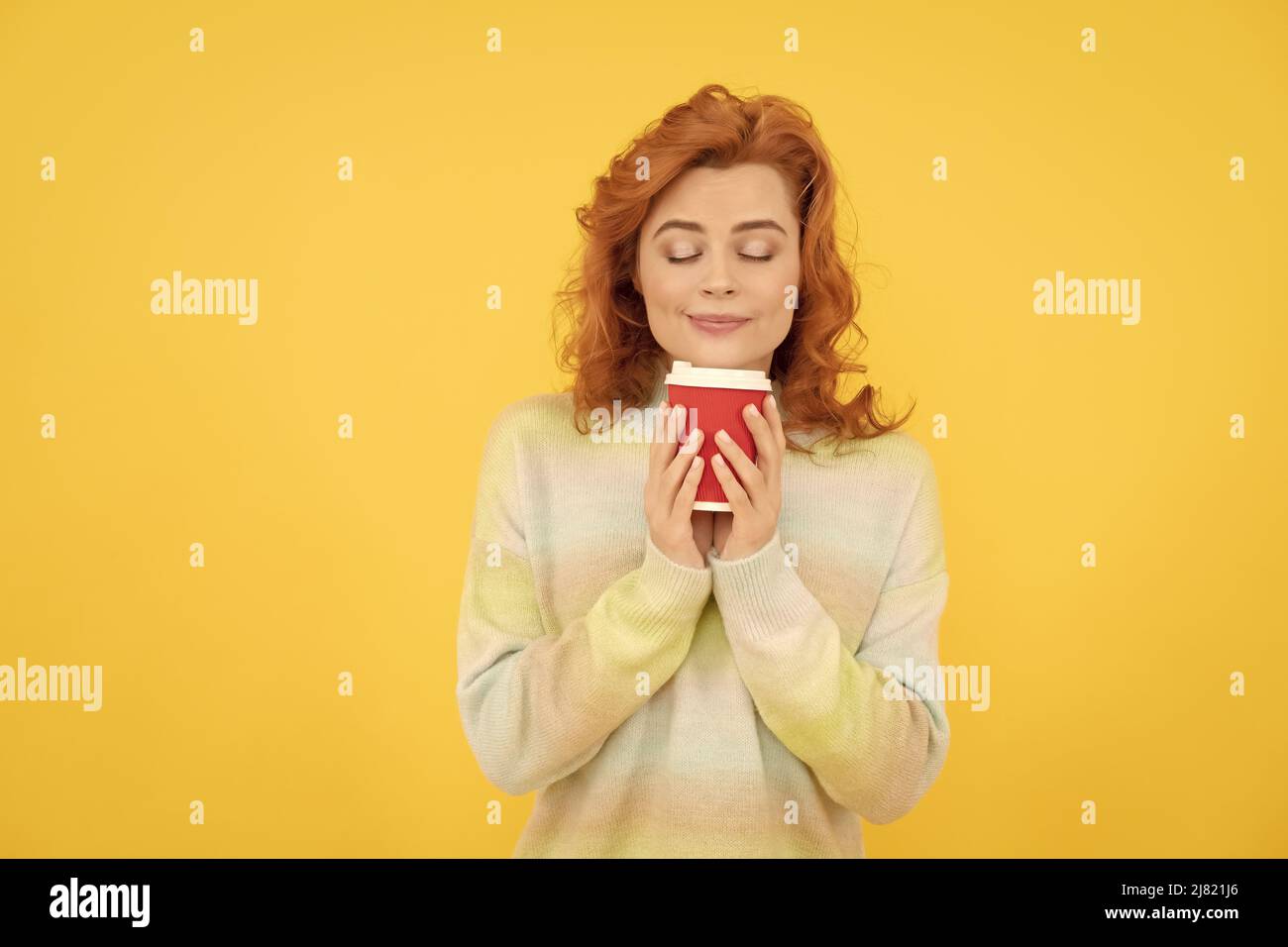 happy redhead woman smelling takeaway coffee from cup on yellow ...