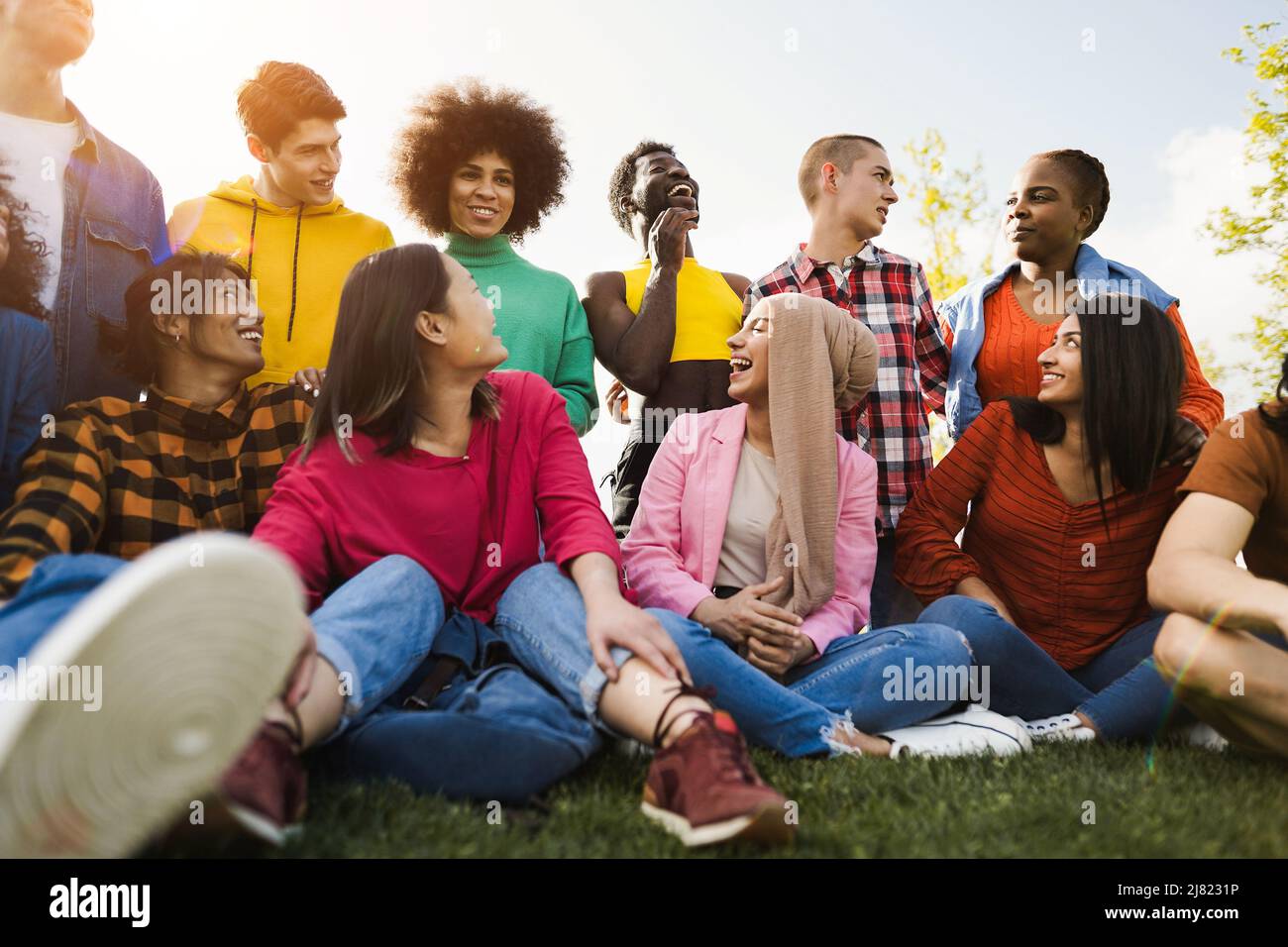Multiethnic diverse people having fun outdoor sitting on grass at city ...