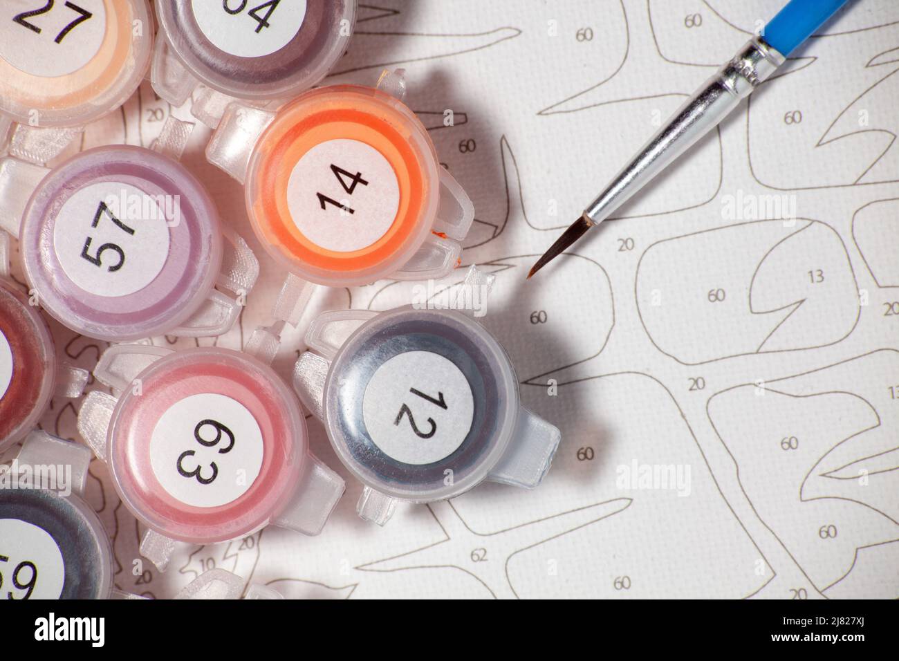 Acrylic paints in jars and paintbrush on canvas with markings ...