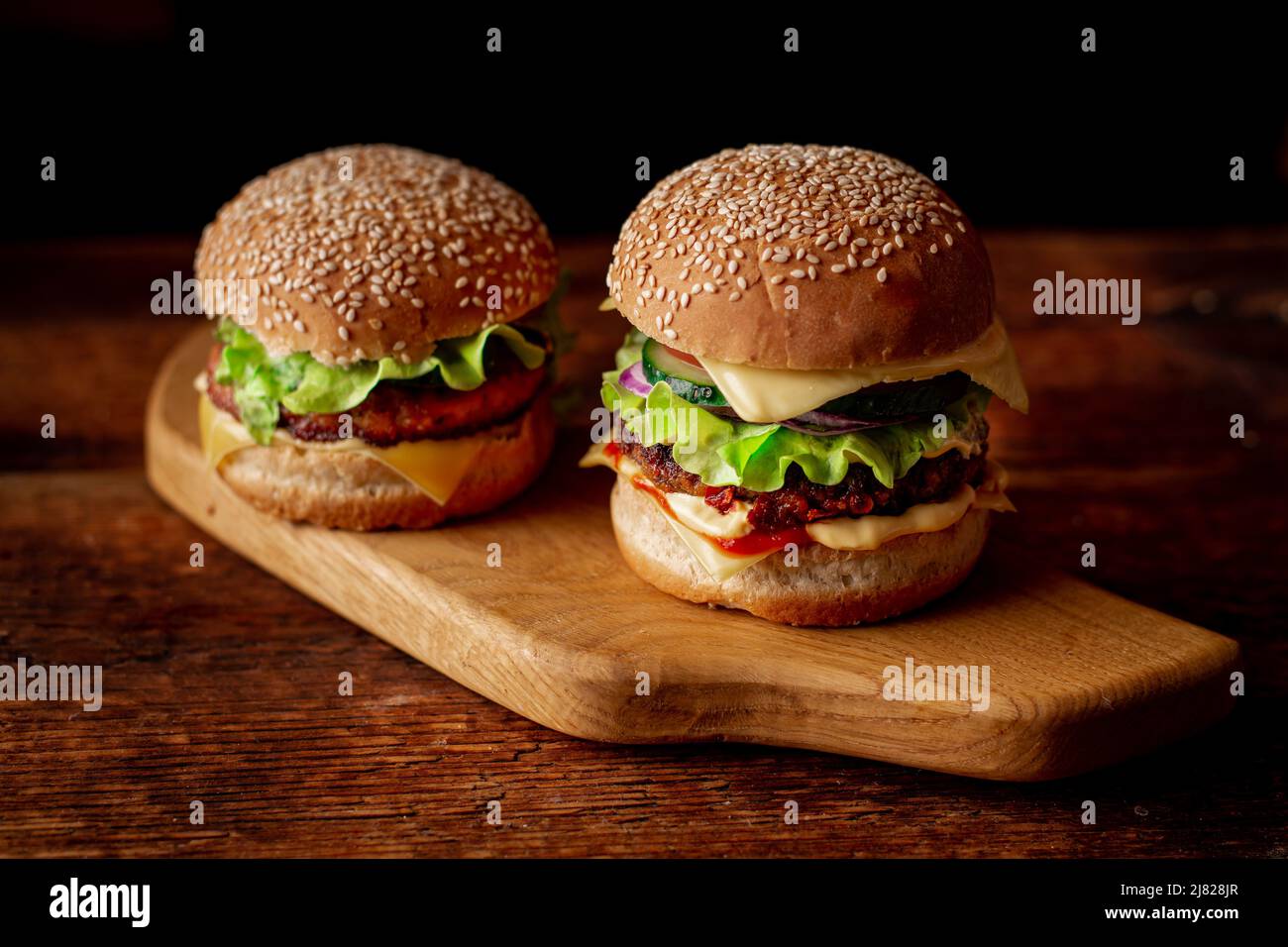 Two hamburgers on a wooden background. Big and small cheeseburger ...