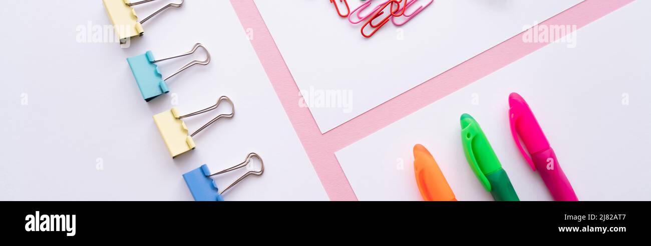 flat lay of colorful fold back clips, paper clips and pens on white ...