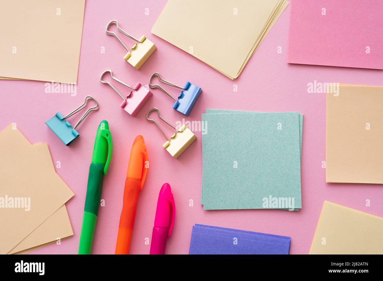 top view of fold back clips near paper notes and colorful pens on pink ...