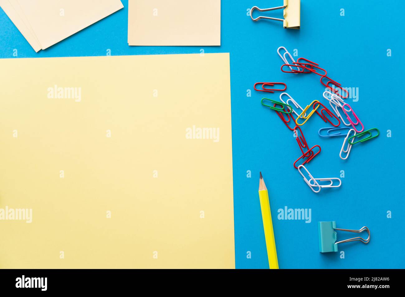 top view of empty papers near colorful paper clips and pencil on blue ...