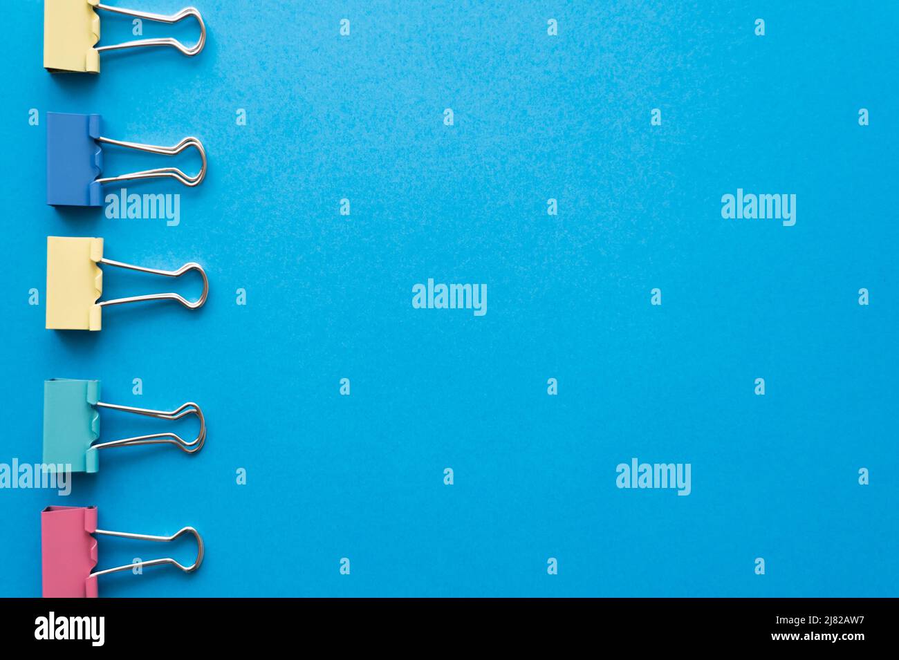top view of colorful pastel fold back clips on blue Stock Photo - Alamy