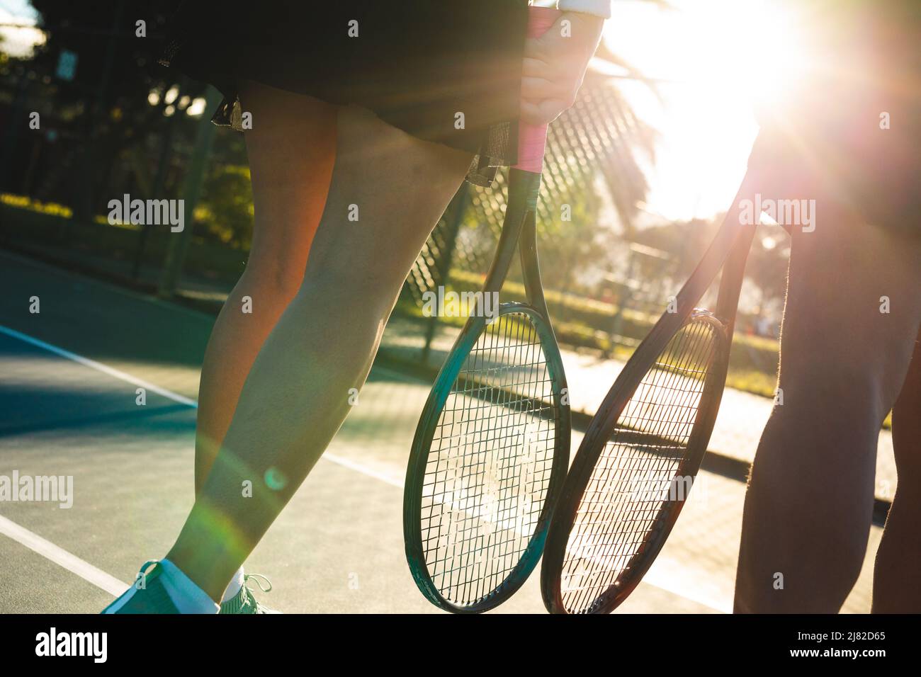 Back lit young female biracial tennis players walking with rackets at ...