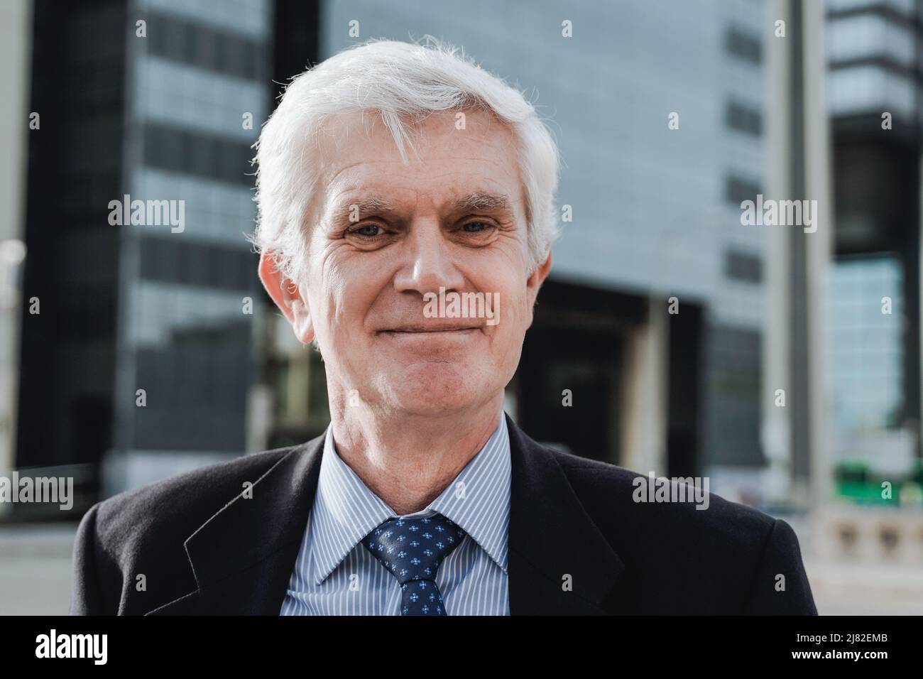 Senior business man looking at camera outdoor with office buildings in ...