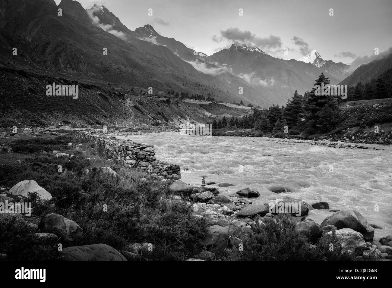 Baspa river flanked by boulders, trees, and the Himalayas with peaks ...