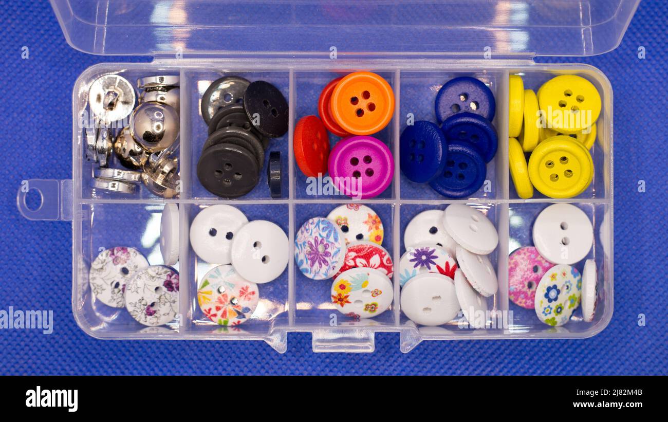 Small buttons for clothes of different types lie cells of a plastic ...