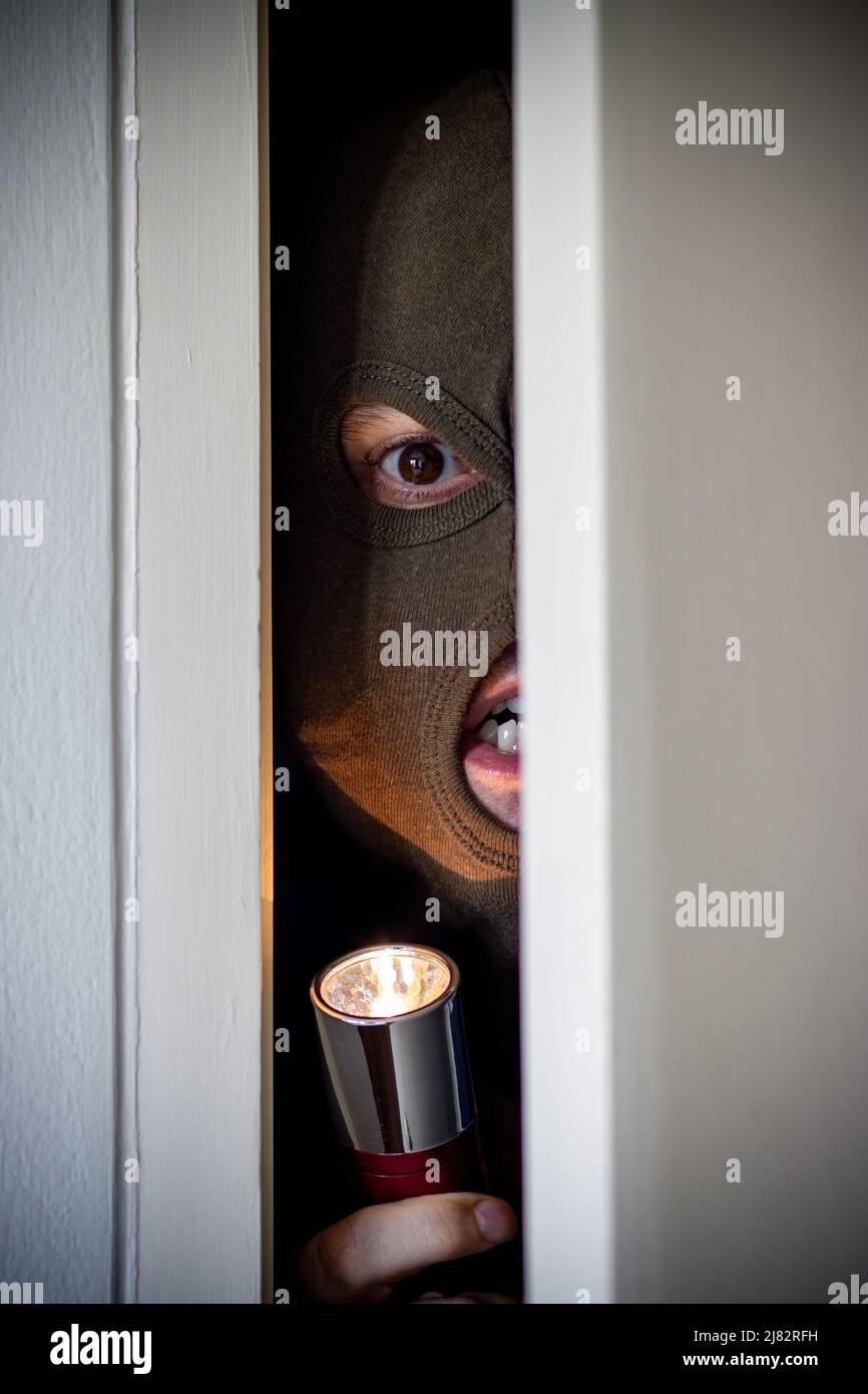 A criminal with a mask on his face opens the door to the room Stock ...