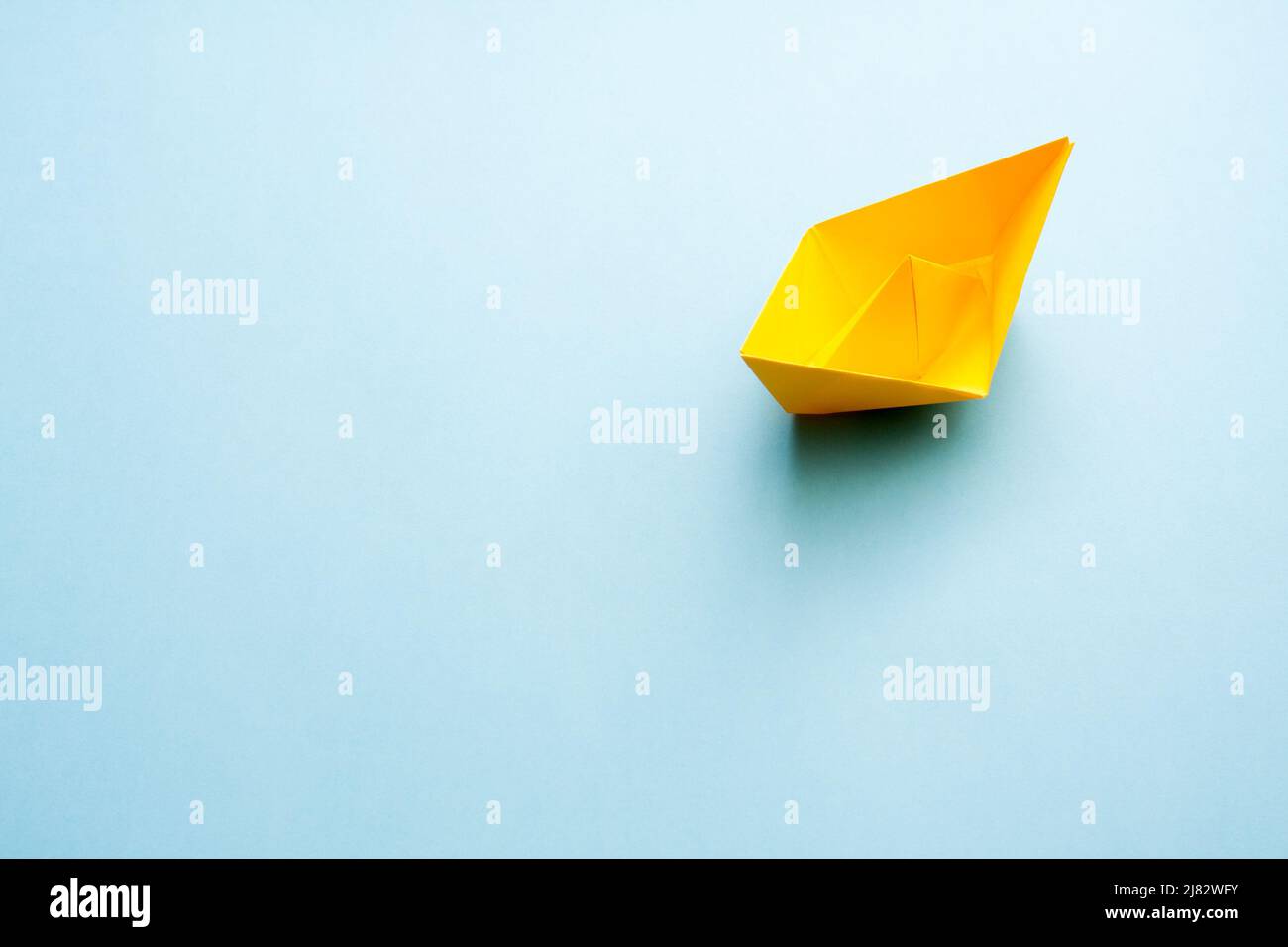 Yellow paper boat on blue background with free copy space for text ...