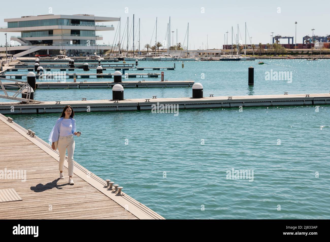 full length view of brunette woman with coffee to go walking on pier in ...
