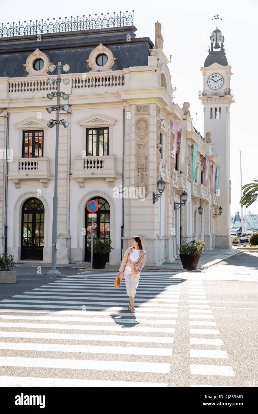 full length of woman walking on crosswalk near building with clock ...