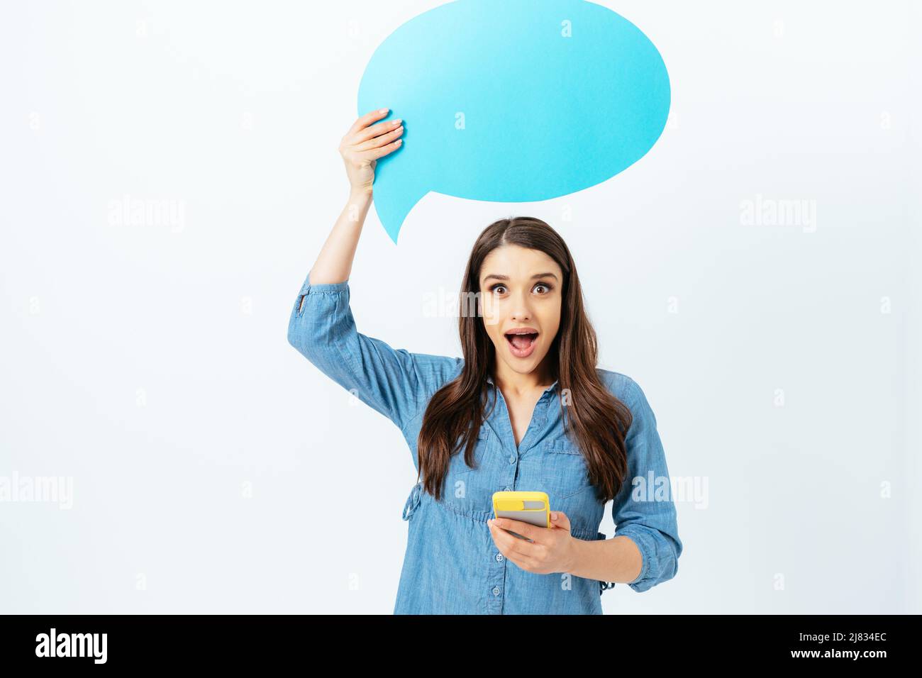 Excited surprised young woman holding smartphone and blank chat box ...