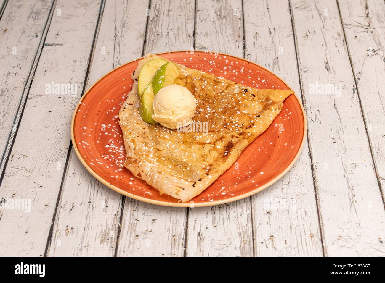 Crepe with icing sugar, vanilla ice cream and green apple slices on a ...