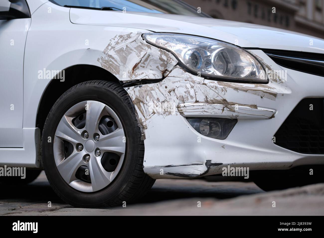 Dented car with damaged fender parked on city street side. Road safety ...