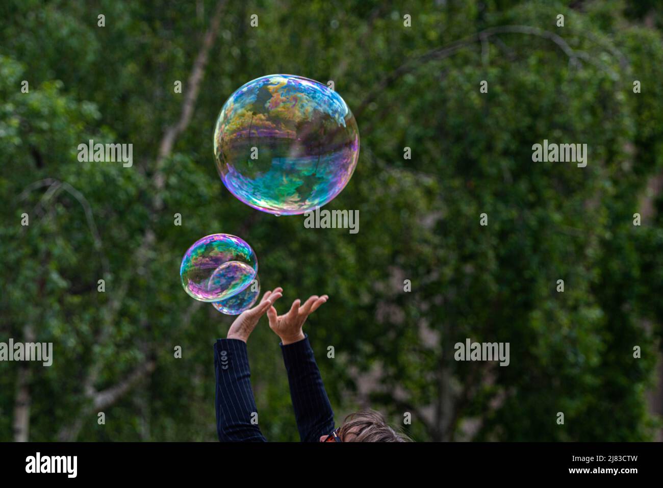 12 May 2022. A hand plays with falling soap bubbles Stock Photo - Alamy