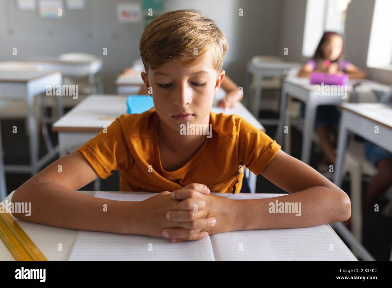 Caucasian elementary schoolboy with hands clasped studying at desk in ...