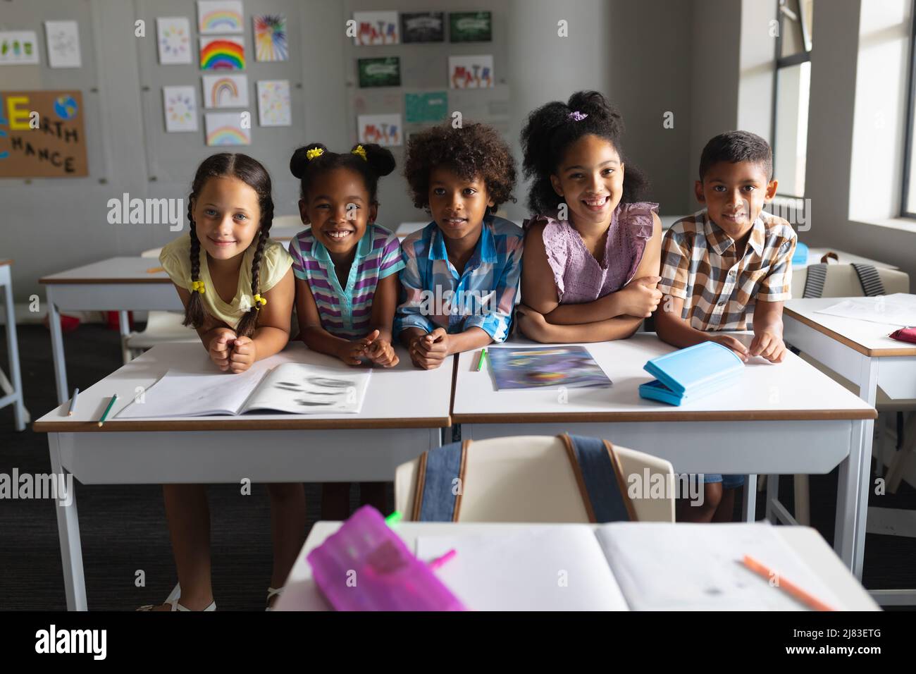 Smiling multiracial elementary school students sitting at desk in ...