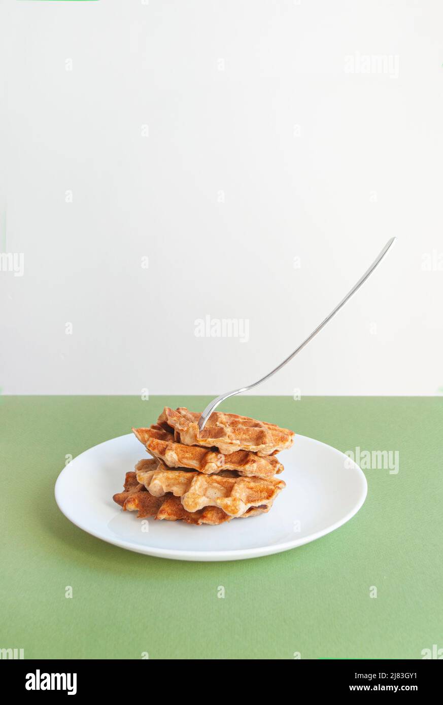 Homemade belgian waffles stack with fork in the middle on a green color ...