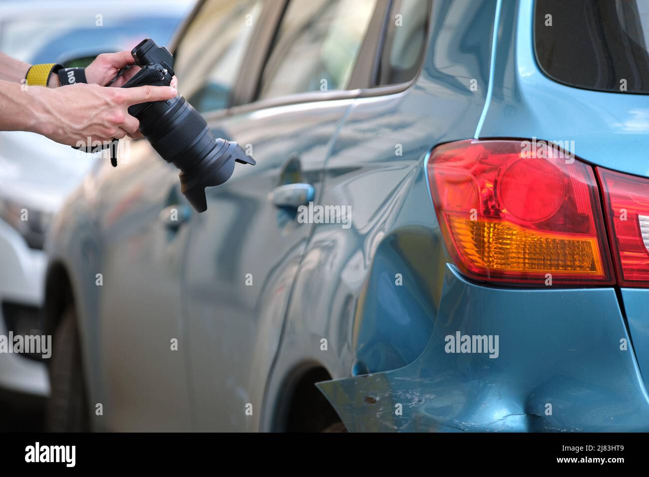 Insurance worker taking photo on camera of dented fender on street side ...