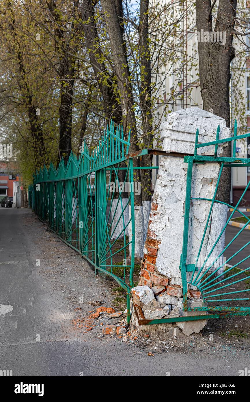 damaged brick column with a metal fence with brick fragments. High ...