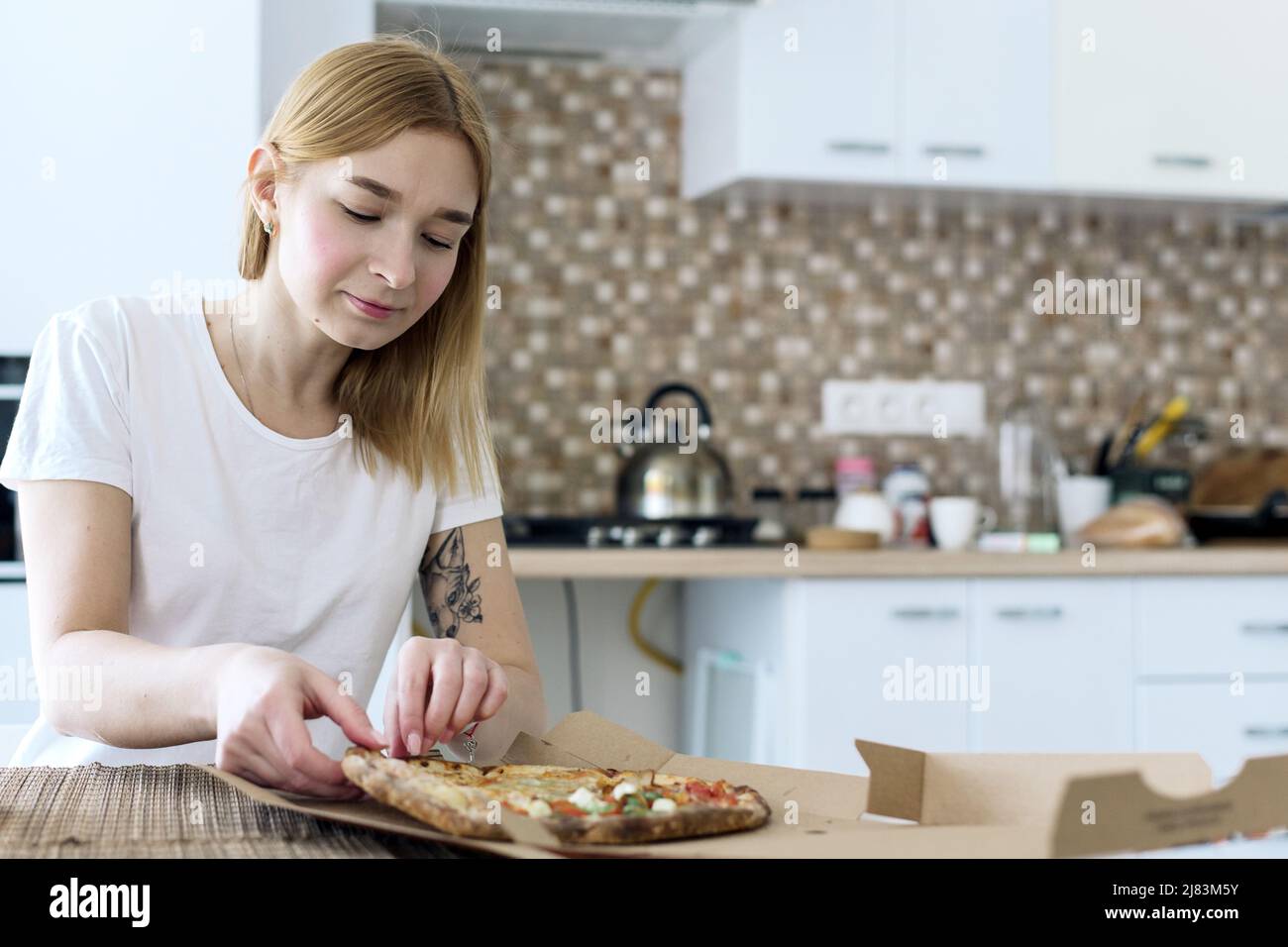 Portrait of a beautiful woman eating pizza in the kitchen. Wrong food ...