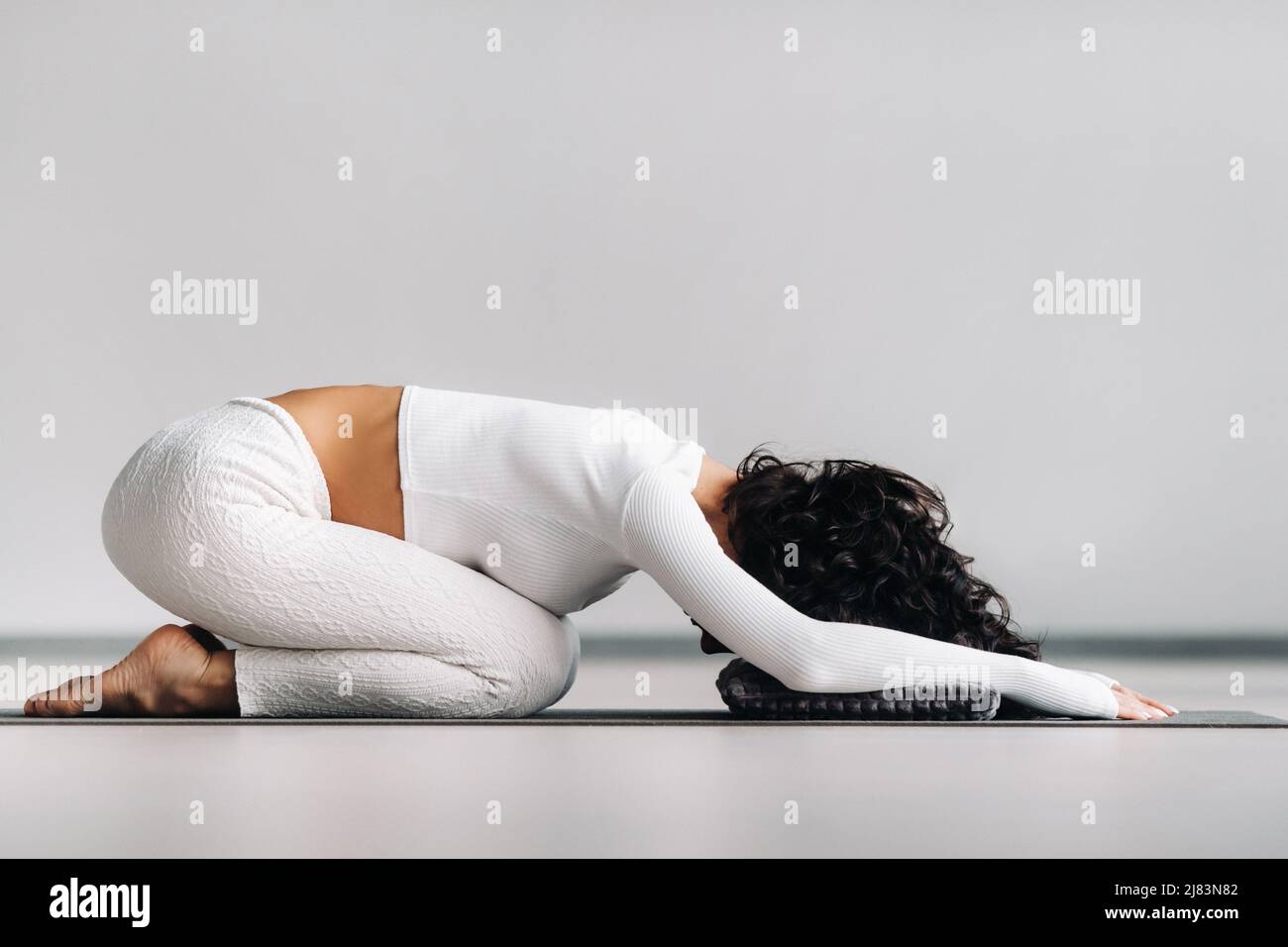 A woman doing yoga on a mat, kneeling makes a bow stretching her arms ...