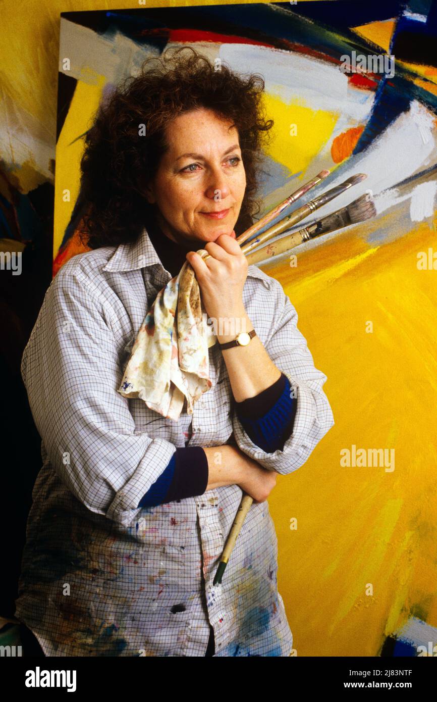1980s MATURE FEMALE ARTIST WITH AN ABSTRACT PAINTING HOLDING BRUSHES ...