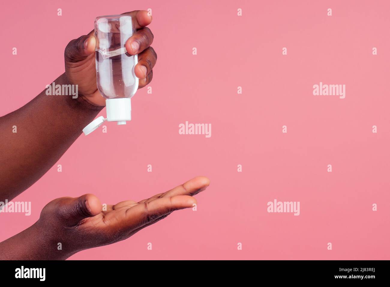 close up hands of dark skinned woman applying alcohol gel in hand pink ...