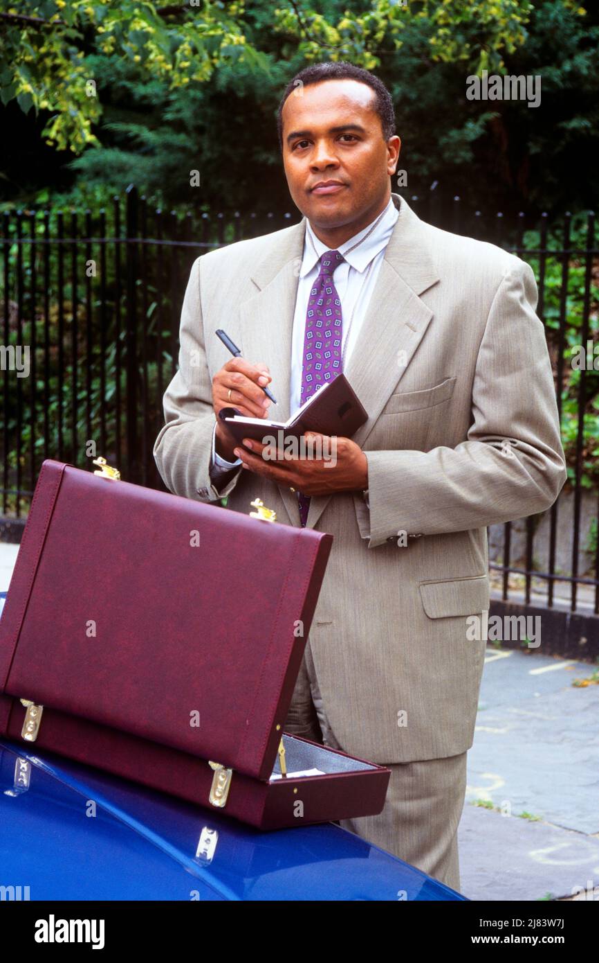 1990s AFRICAN-AMERICAN SALESMAN CHECKING NOTES BEFORE MEETING CLIENT ...