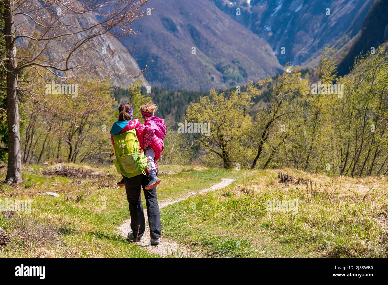 Mother holding his daughter in embrace while walking on forest meadow ...