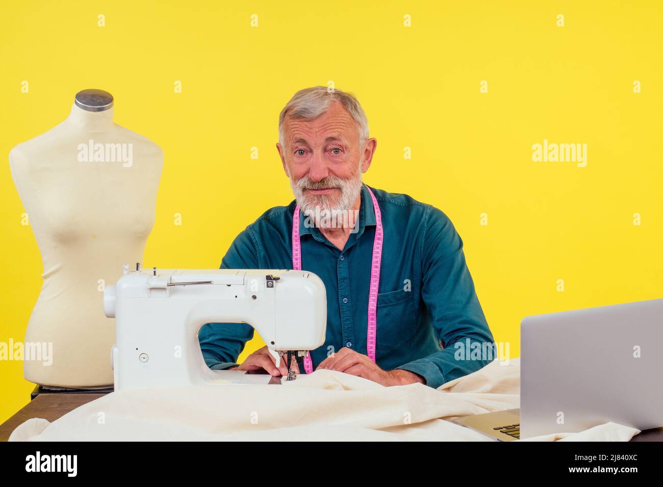 pleasing old man working in tailoring studio making clothes at sewing ...