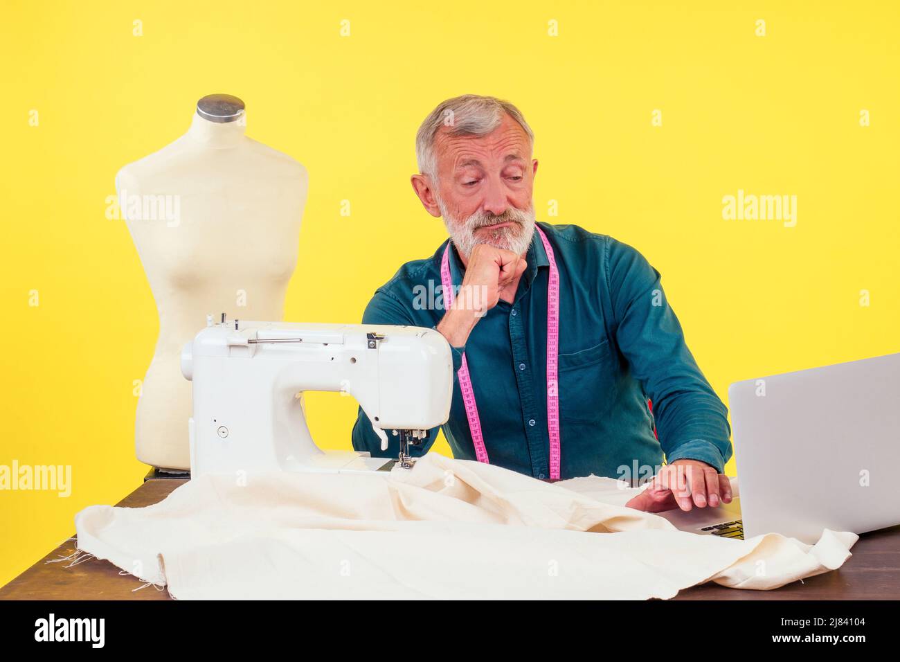 pleasing old man working in tailoring studio making clothes at sewing ...