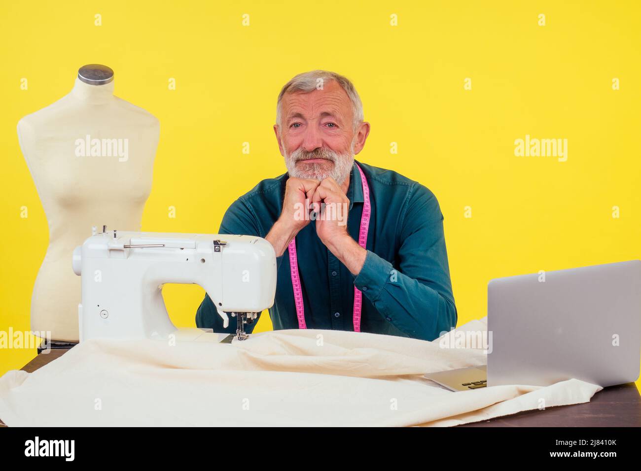 pleasing old man working in tailoring studio making clothes at sewing ...