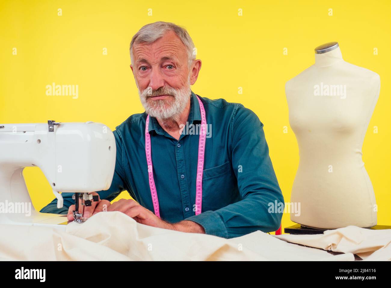 pleasing old man working in tailoring studio making clothes at sewing ...