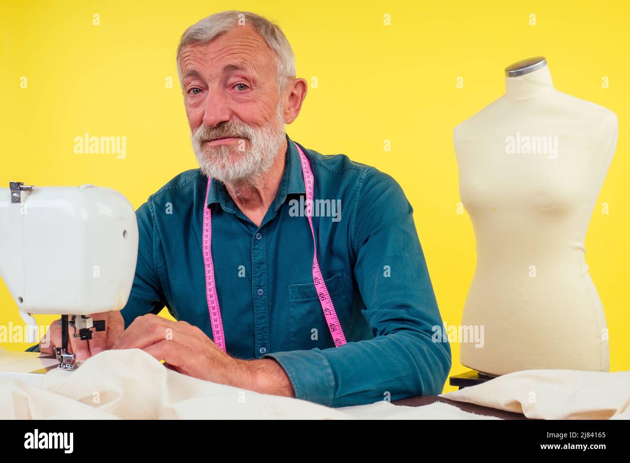 pleasing old man working in tailoring studio making clothes at sewing ...