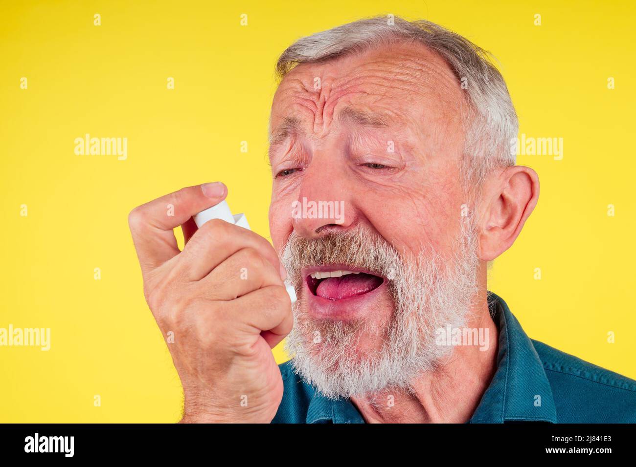 Senior man using an asthma inhaler in studio yellow background Stock ...