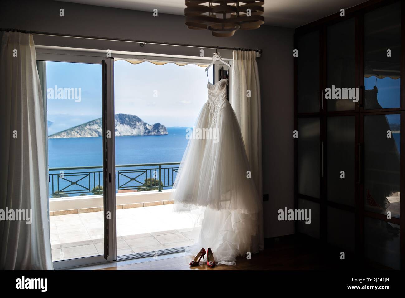Wedding dress hanging on the window in the room Stock Photo - Alamy