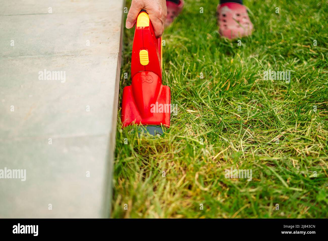 Close up of man hand with red hedge trimmer cutting green grass at ...