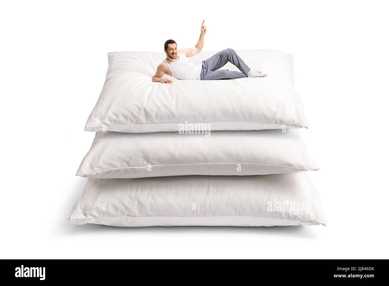 Young man lying on a pile of pillows in pajamas and pointing above ...