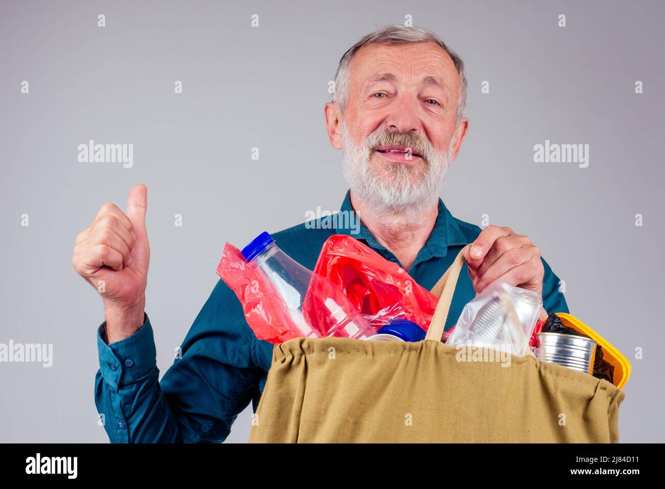 old grandfather holding cotton eco bag full of garbage in studio white ...