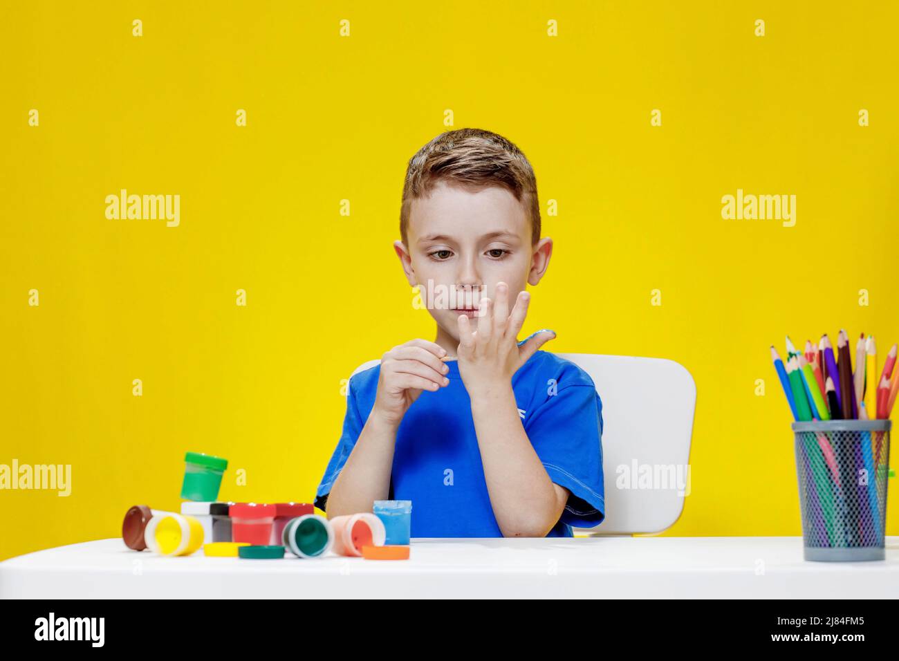 A little preschooler sits at a table, holding a brush in his hand and ...